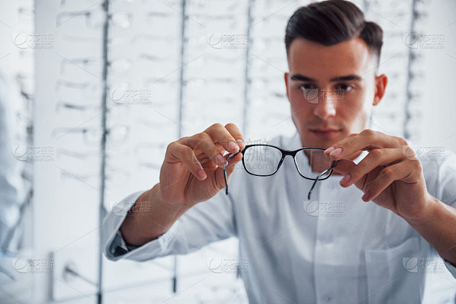 室内年轻眼科医生手持的全新眼镜聚焦照片