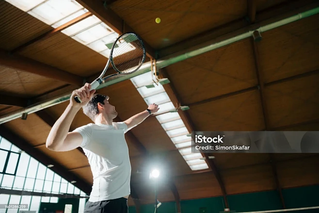 Young male instructor throwing ball up in air and hitting serve on ...
