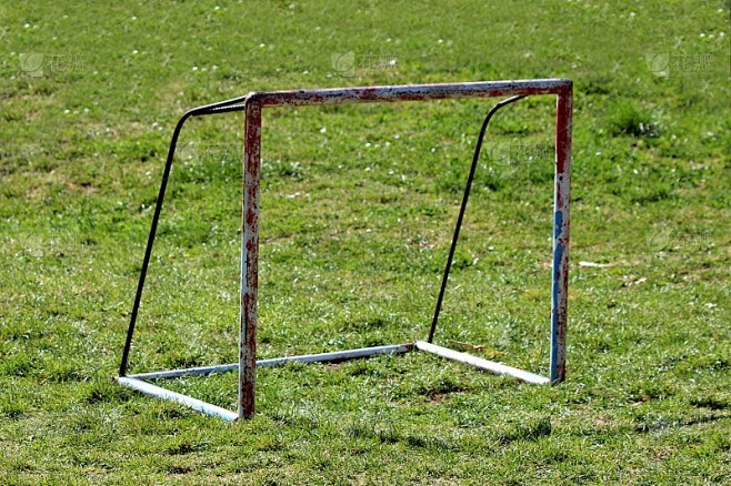 锈迹斑斑的旧金属门柱周围是未修剪的草地，等待修复和油漆当地的操场