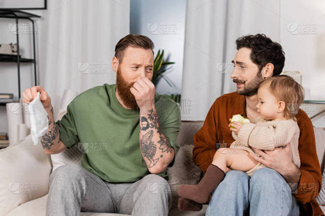 Disgusted gay man plugging nose while holding diap