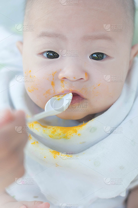 肮脏的亚洲婴儿用勺子喂养