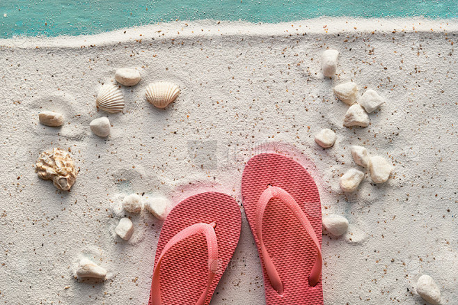 粉色橡胶人字拖，沙滩上的拖鞋，海边的石头，工作室的概念。白色的沙子，白色的石头和蓝色的背景