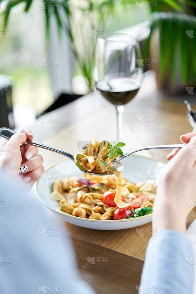 女人吃意大利意大利面，海鲜和番茄酱。意大利面甘贝里尼。特写标签用勺子绕着叉子转。帕尔马奶酪