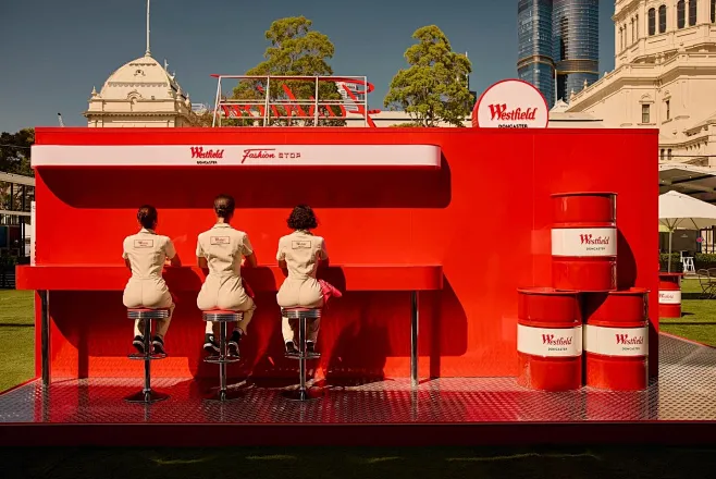 This may contain: two men sitting on stools in front of a large red ...