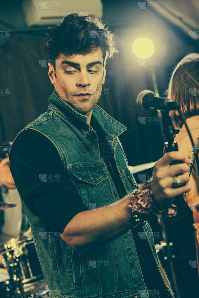 英俊的歌手站在摇滚乐队附近的麦克风