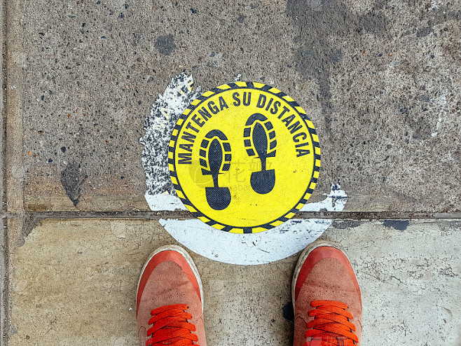 地板上有保持社交距离的标志，上面用西班牙语写着:保持距离站在这里。当地商店入口处的标志。COVID-