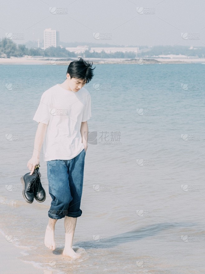 年轻男性拿着鞋挽起裤脚走在海边的沙滩上